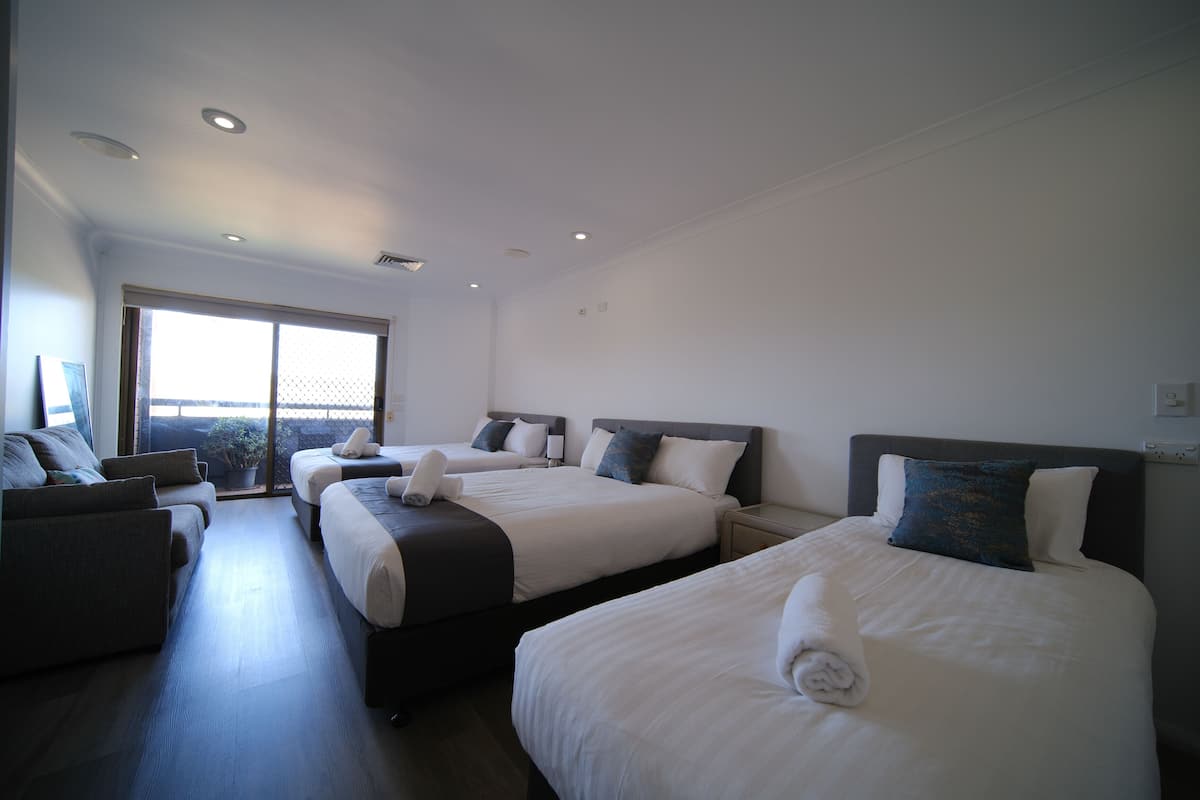 Quarto de hotel com três camas, um sofá e uma janela grande.