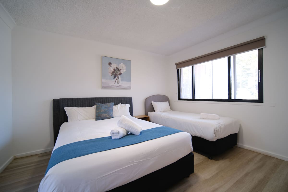 Quarto de hotel com duas camas, uma janela grande e um quadro na parede.