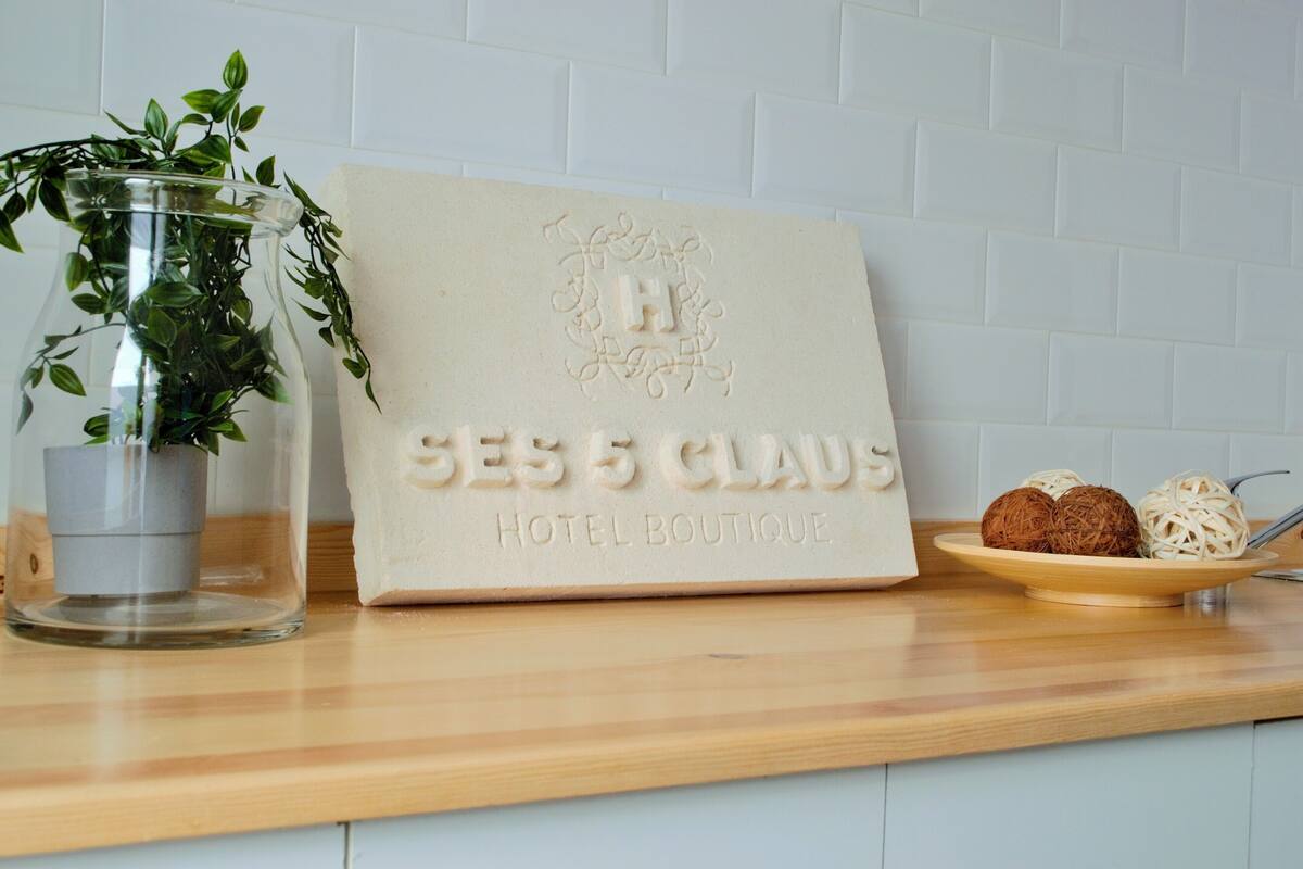 Um letreiro de hotel com a inscrição 'SES 5 CLAUS HOTEL BOUTIQUE' e uma mesa de madeira com uma planta e um prato de comida.