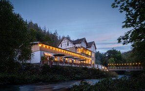 Um edifício tradicional em estilo de enxaimel com área de estar ao ar livre e um rio ao primeiro plano.