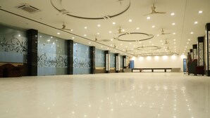 Um hall de hotel espaçoso e bem iluminado, com piso polido, painéis decorativos e ventiladores de teto.