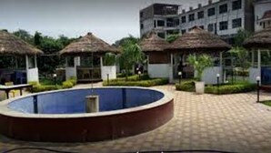 Uma área de piscina com uma piscina circular, estruturas com telhados de palha e um edifício ao fundo.