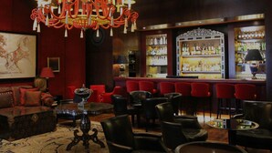 Uma área de bar com cadeiras vermelhas, balcão e um candelabro.