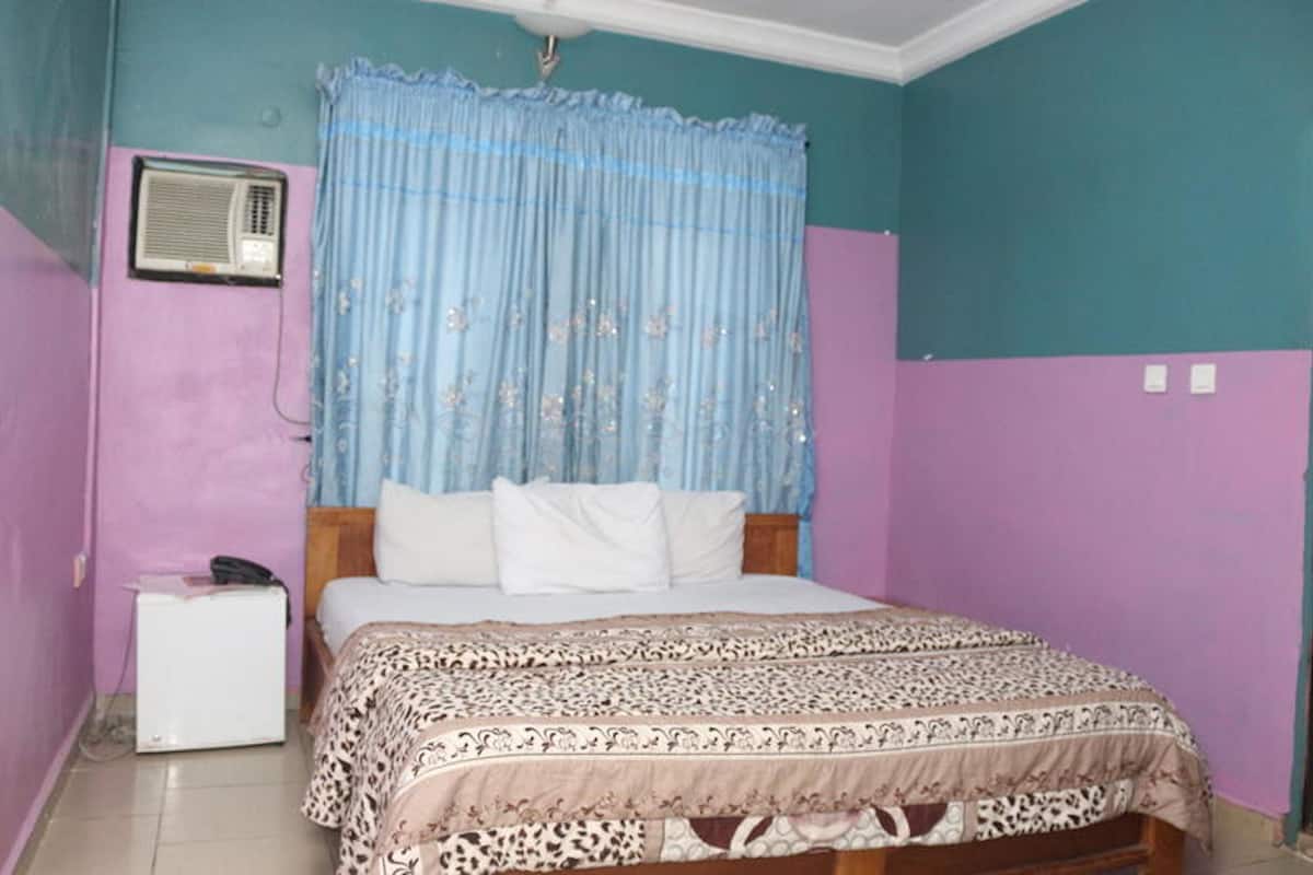 Quarto com cama, mesa de cabeceira, aquecedor e janela com cortinas.