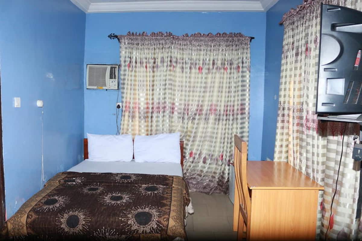 Quarto com cama, mesa de madeira, televisão e janela com cortinas.