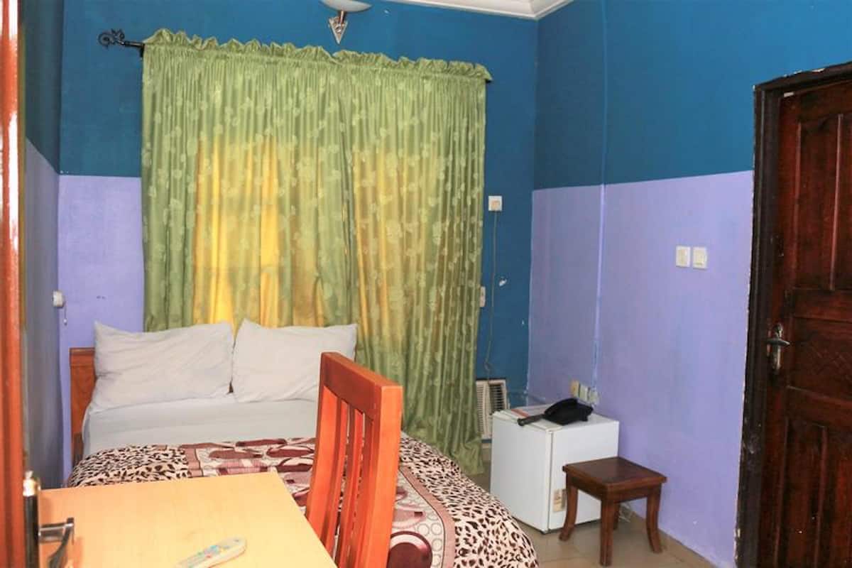 Um quarto com uma cama, uma mesinha, uma cadeira, uma escrivaninha e um armário.