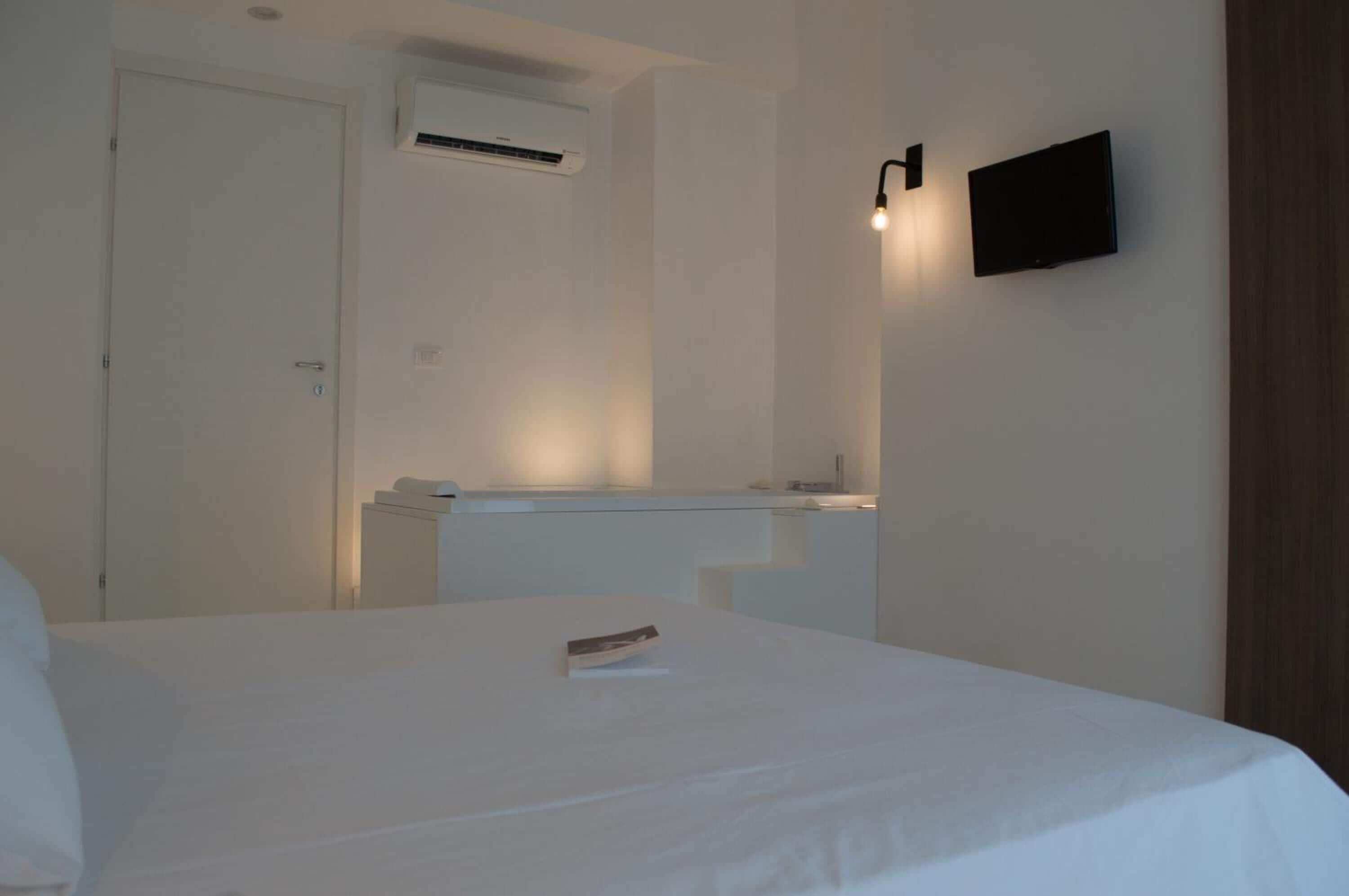 Quarto de hotel com uma cama, televisão de tela plana na parede, mesa de cabeceira e pequena escrivaninha com cadeira.