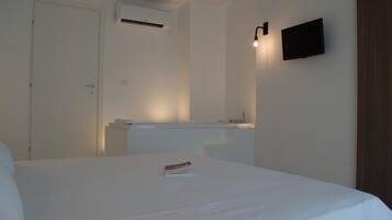 Quarto de hotel com uma cama, televisão de tela plana na parede, mesa de cabeceira e pequena escrivaninha com cadeira.