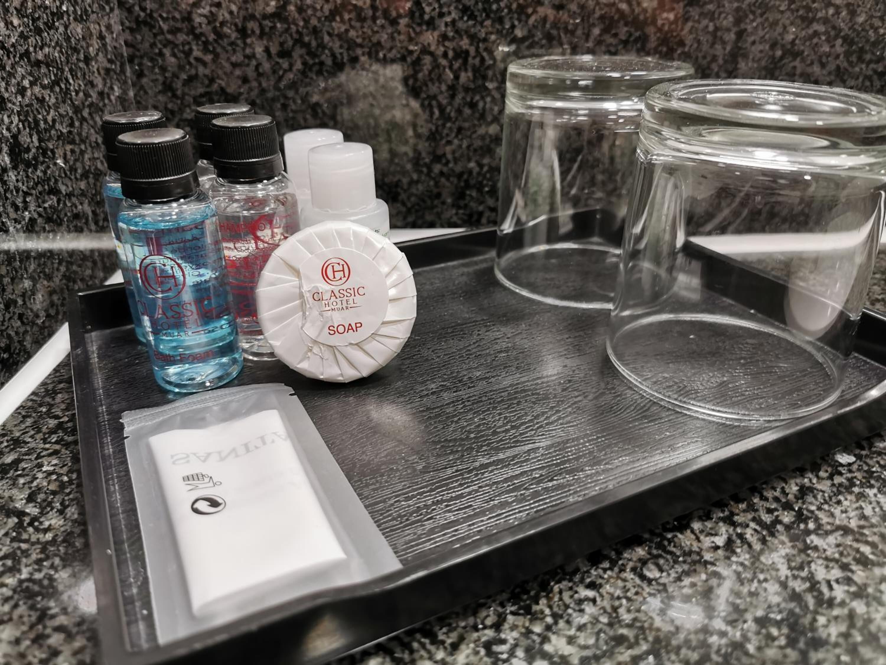 Uma bandeja com artigos de higiene pessoal, incluindo uma garrafa de líquido azul, um sabonete branco e uma embalagem branca, provavelmente contendo uma lâmina de barbear.