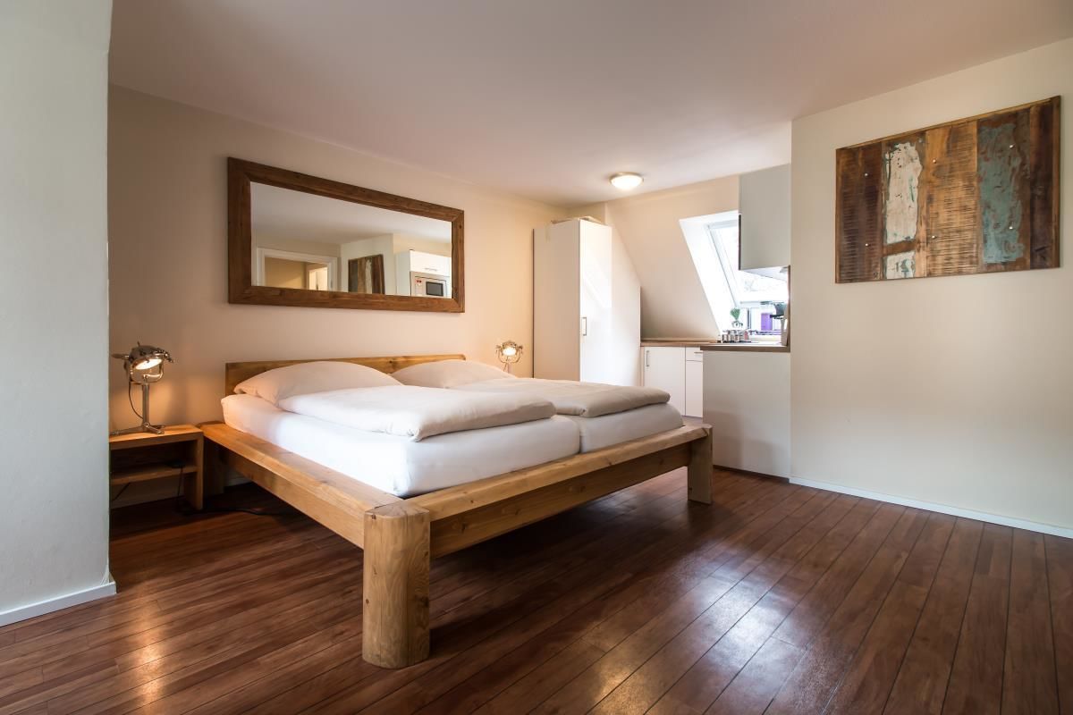 Um quarto com uma cama de madeira, uma mesa de cabeceira, um espelho e um quadro na parede.