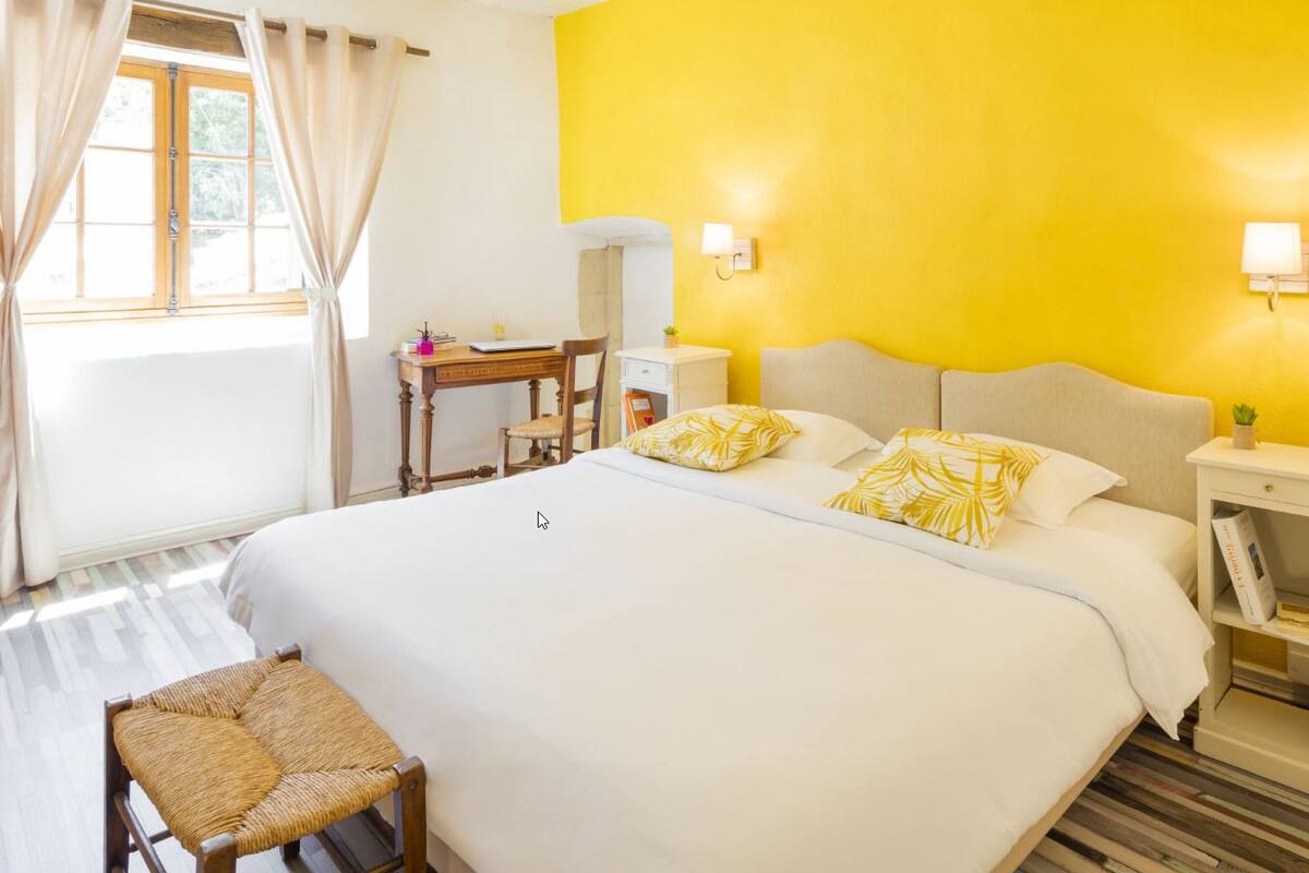 Quarto de hotel com uma cama grande, uma escrivaninha, uma cadeira e uma mesa de cabeceira com abajur.