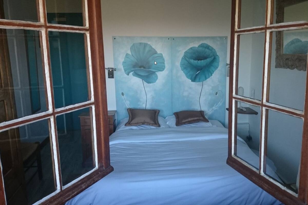 Quarto com uma cama, duas almofadas e uma parede com um grande quadro de flores.