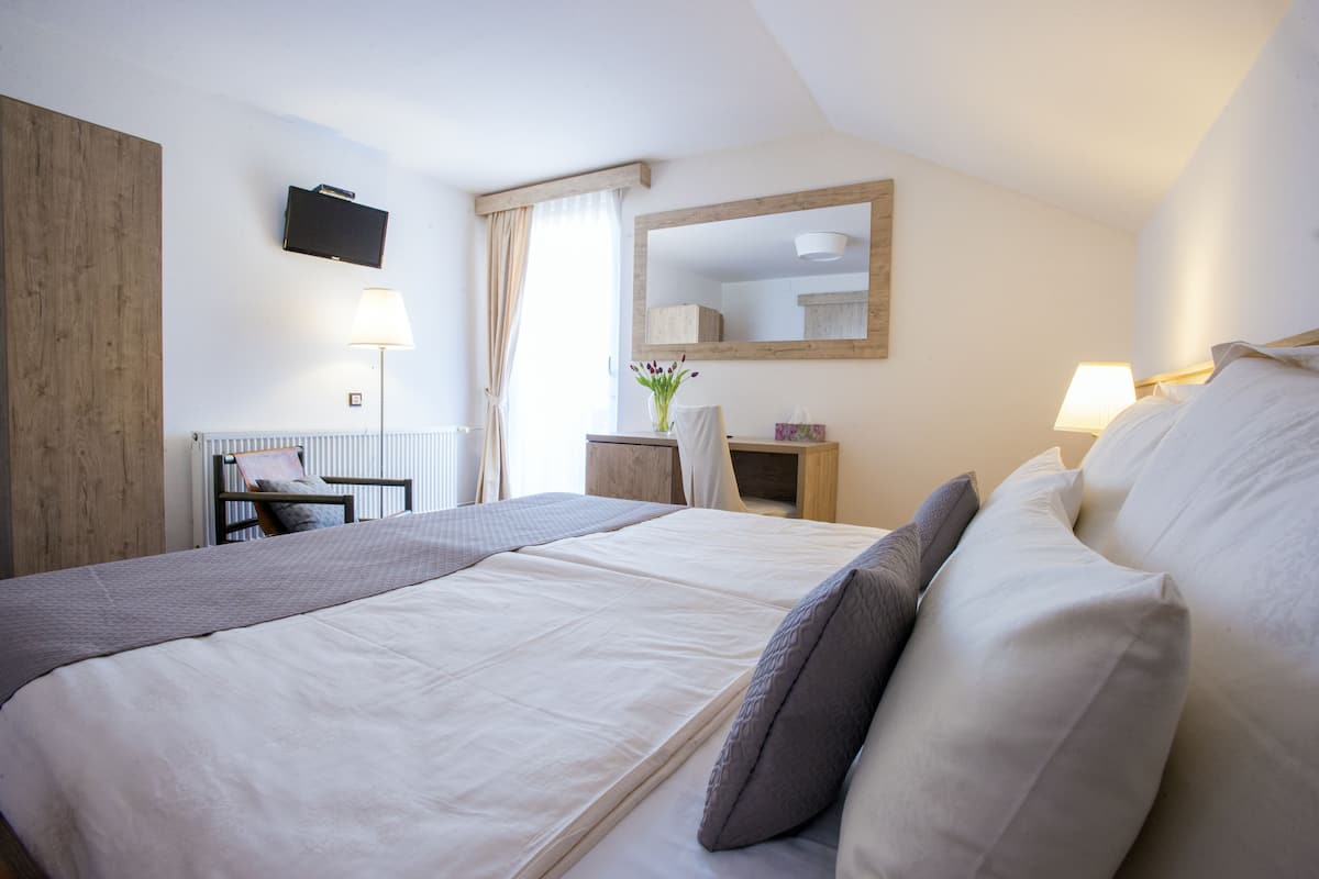 Quarto de hotel com uma cama grande, uma escrivaninha, uma cadeira, um espelho e uma TV fixada na parede.