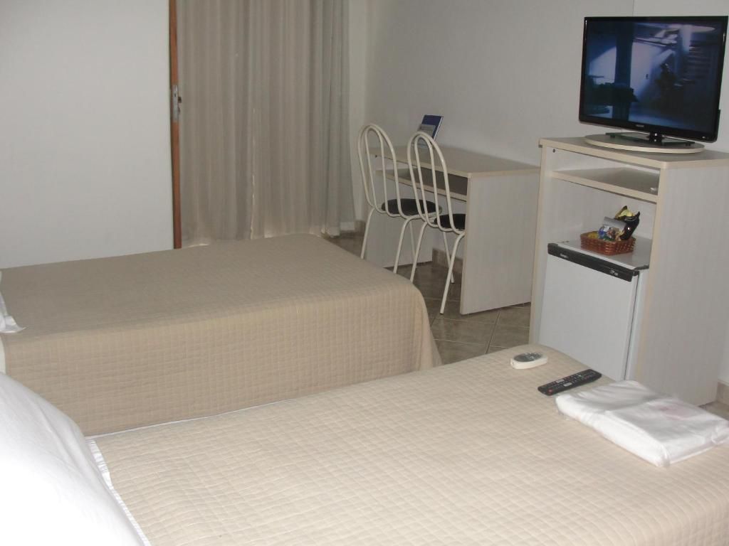 Quarto de hotel com duas camas, uma escrivaninha, uma cadeira, uma televisão e um controle remoto.