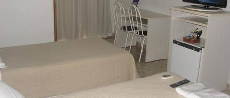 Quarto de hotel com duas camas, uma escrivaninha, uma cadeira, uma televisão e um controle remoto.