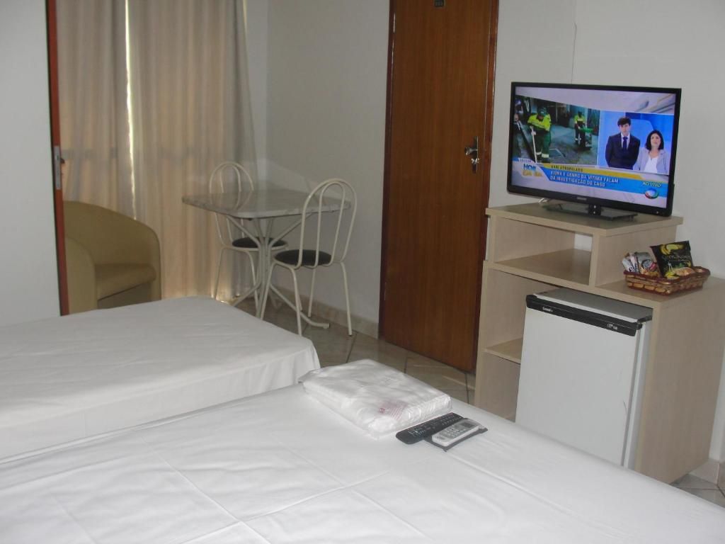 Quarto de hotel com duas camas, televisão, pequena geladeira, escrivaninha e uma cadeira.