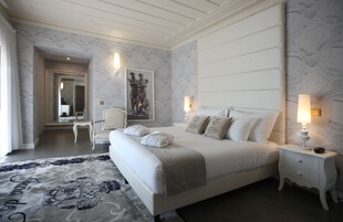 Um quarto com uma cama grande, mesas de cabeceira, uma cadeira, um espelho e um quadro na parede.