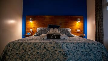 Uma cama bem arrumada com um edredom estampado com motivos florais, uma mesa de cabeceira com abajur e uma cabeceira de madeira.
