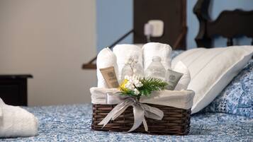 Uma cesta de vime com produtos de higiene e toalhas sobre uma cama com colcha azul estampada.