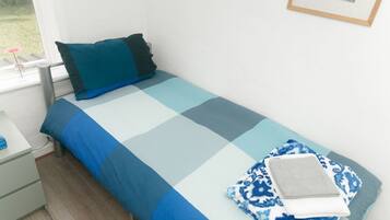 Uma cama bem arrumada com colcha xadrez azul e cinza, travesseiro estampado em azul e branco, e um quadro na parede.