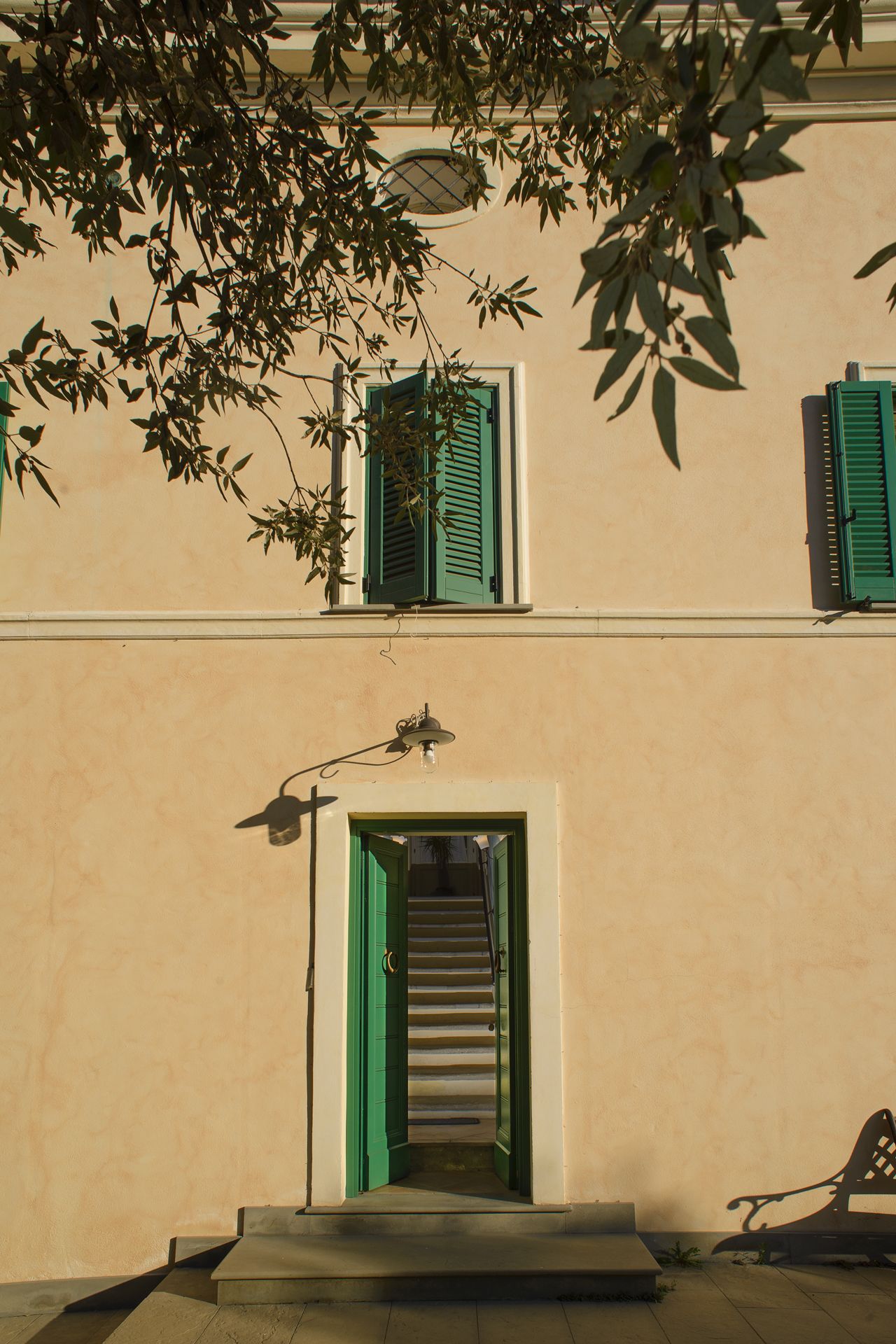 Um edifício com fachada bege, porta verde e escadaria que leva a um andar superior.
