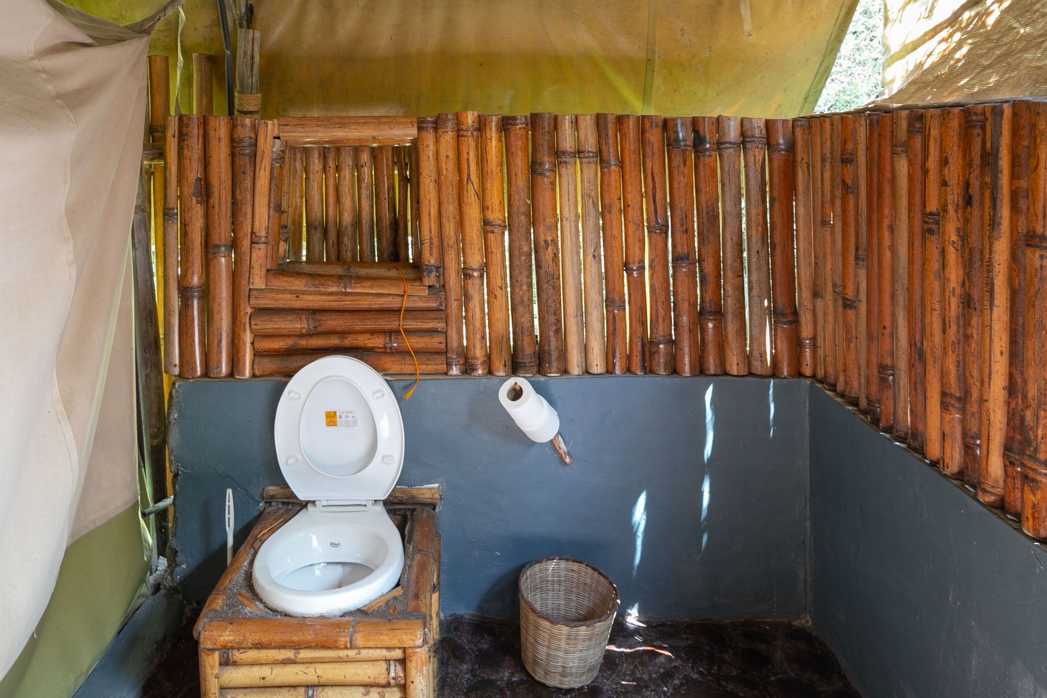 Casa de banho com paredes de bambu, com uma sanita e uma cesta.