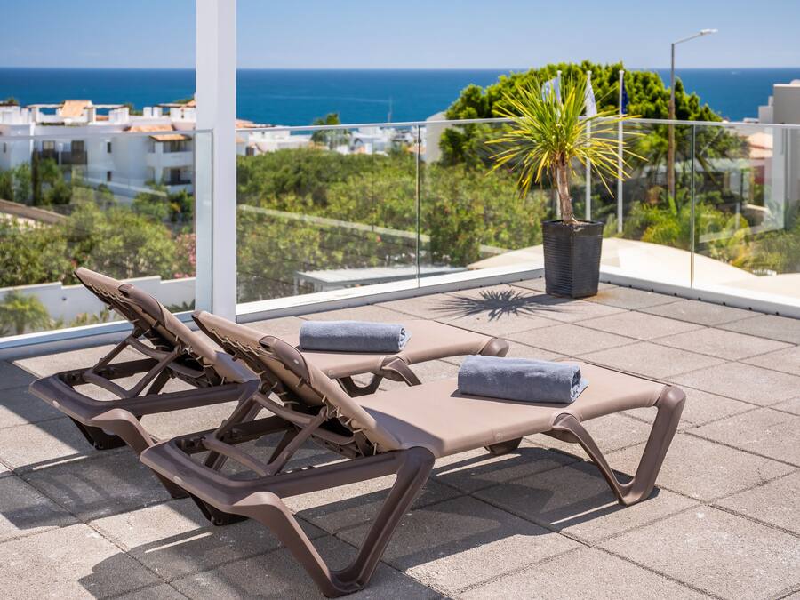 Terraço no telhado com duas espreguiçadeiras, um vaso de planta e vista para o mar e edifícios.