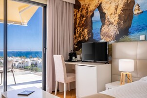 Quarto de hotel com escrivaninha, televisão, luminária e cama.
