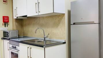 Uma cozinha compacta com armários brancos, micro-ondas embutido, geladeira de aço inoxidável e pia com torneira.