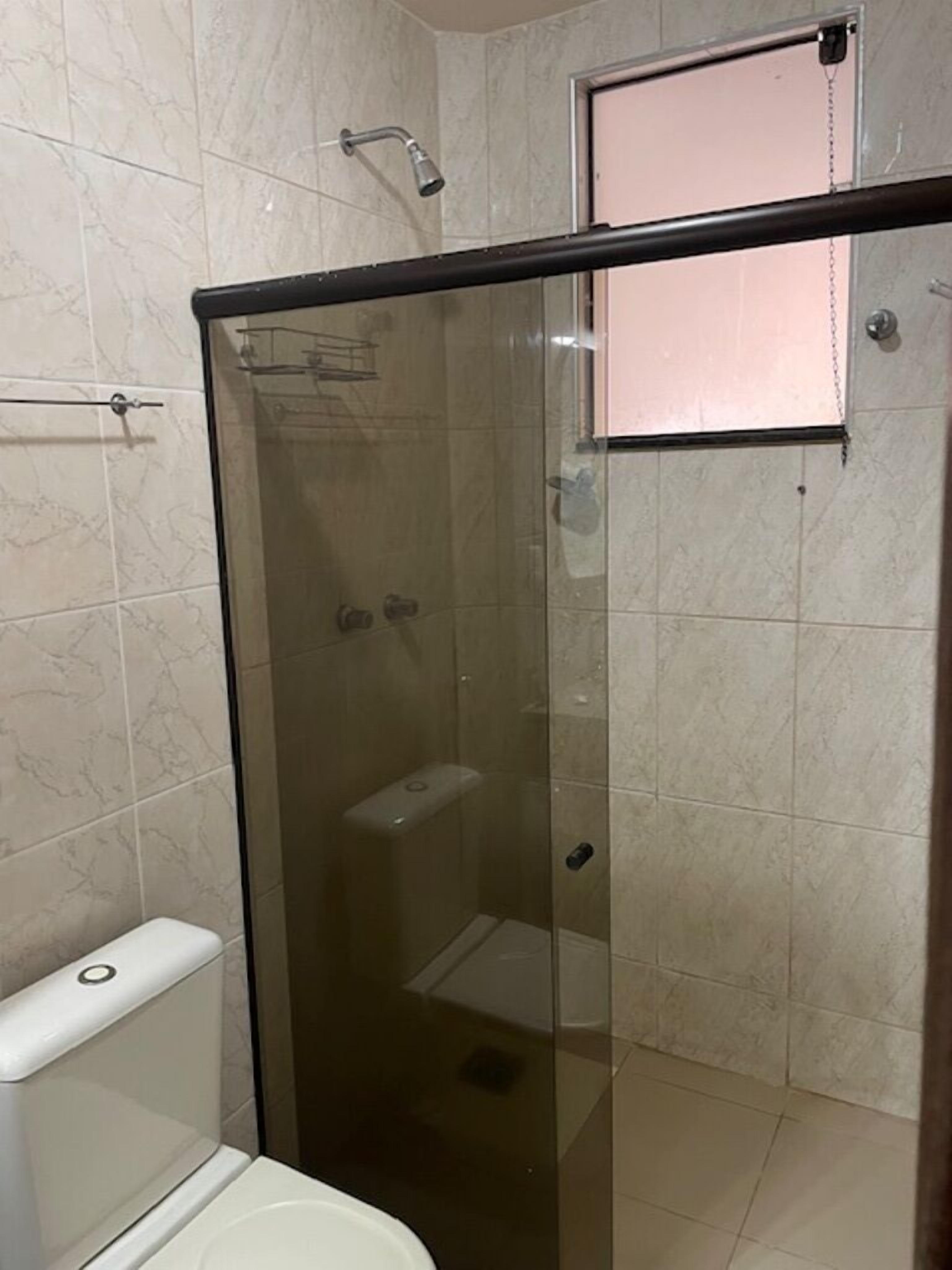 Divisória de chuveiro envidraçada com vaso sanitário à esquerda.