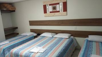 Quarto de hotel com duas camas, cabeceira de madeira, decoração na parede e uma prateleira com um objeto enrolado.