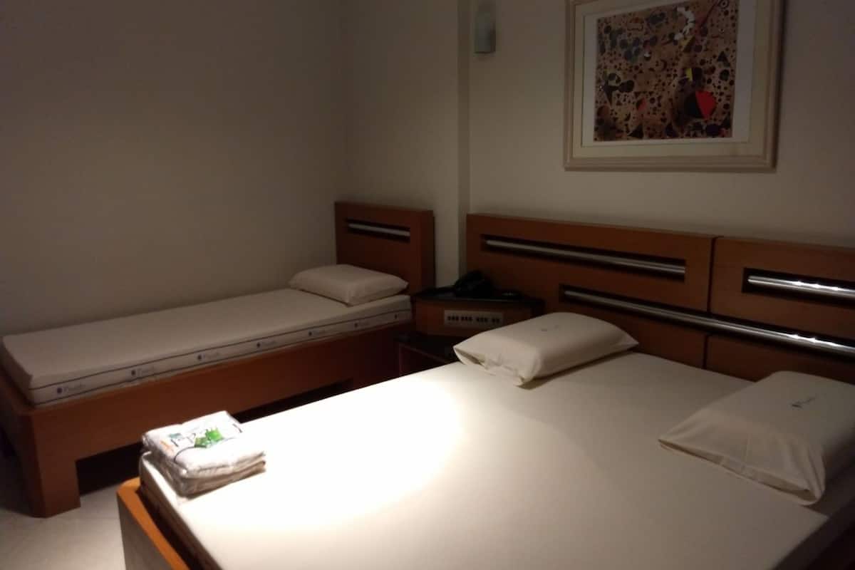 Quarto com uma cama de solteiro, mesa de cabeceira e um quadro abstrato na parede.