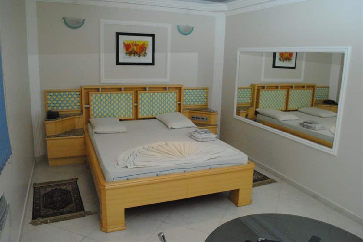 Um quarto com cama de madeira, duas mesas de cabeceira, um espelho e um quadro pendurado na parede.