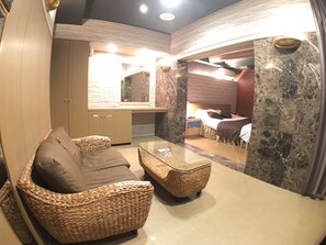 Um quarto com sofá de fibra natural, mesa de centro de vidro e cama com cabeceira.