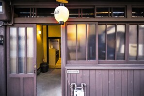 Entrada de um edifício japonês tradicional com porta de madeira, um lança-luz e espaço interior visível, incluindo um balcão e bancos.