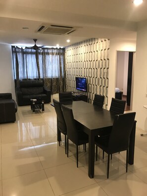 Uma sala de estar moderna com um sofá de couro escuro, uma mesa de jantar com cadeiras, uma TV de tela plana fixada em uma parede estampada e um ventilador de teto.