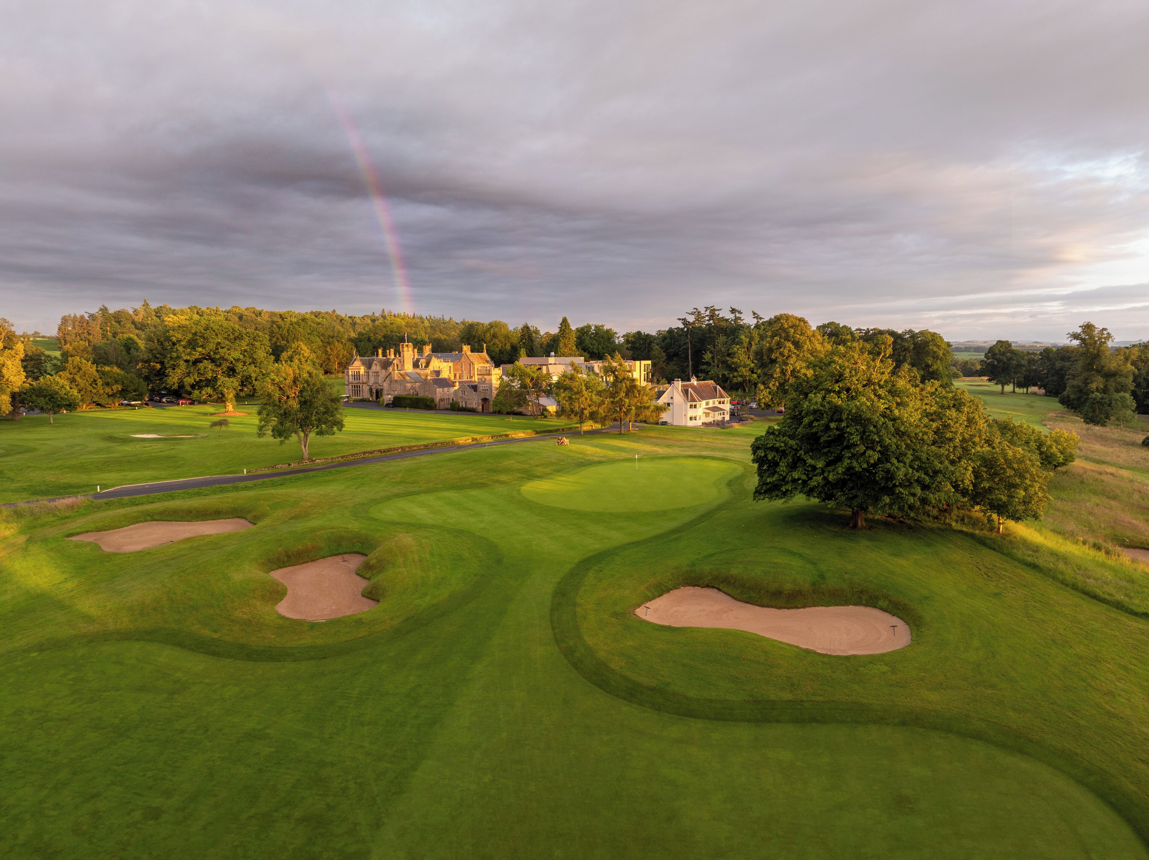 Um campo de golfe com bunkers de areia, um clube e uma grande propriedade ao fundo.