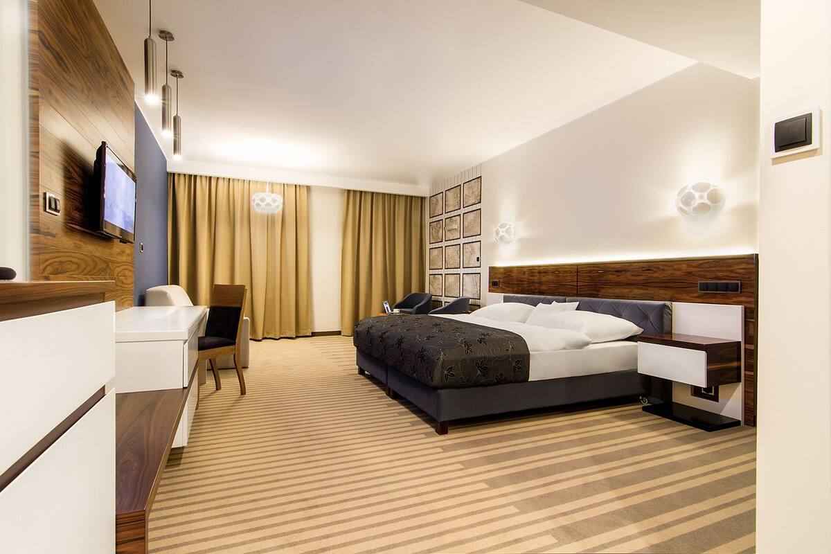 Quarto de hotel moderno com uma cama grande, uma escrivaninha e uma televisão presa à parede.