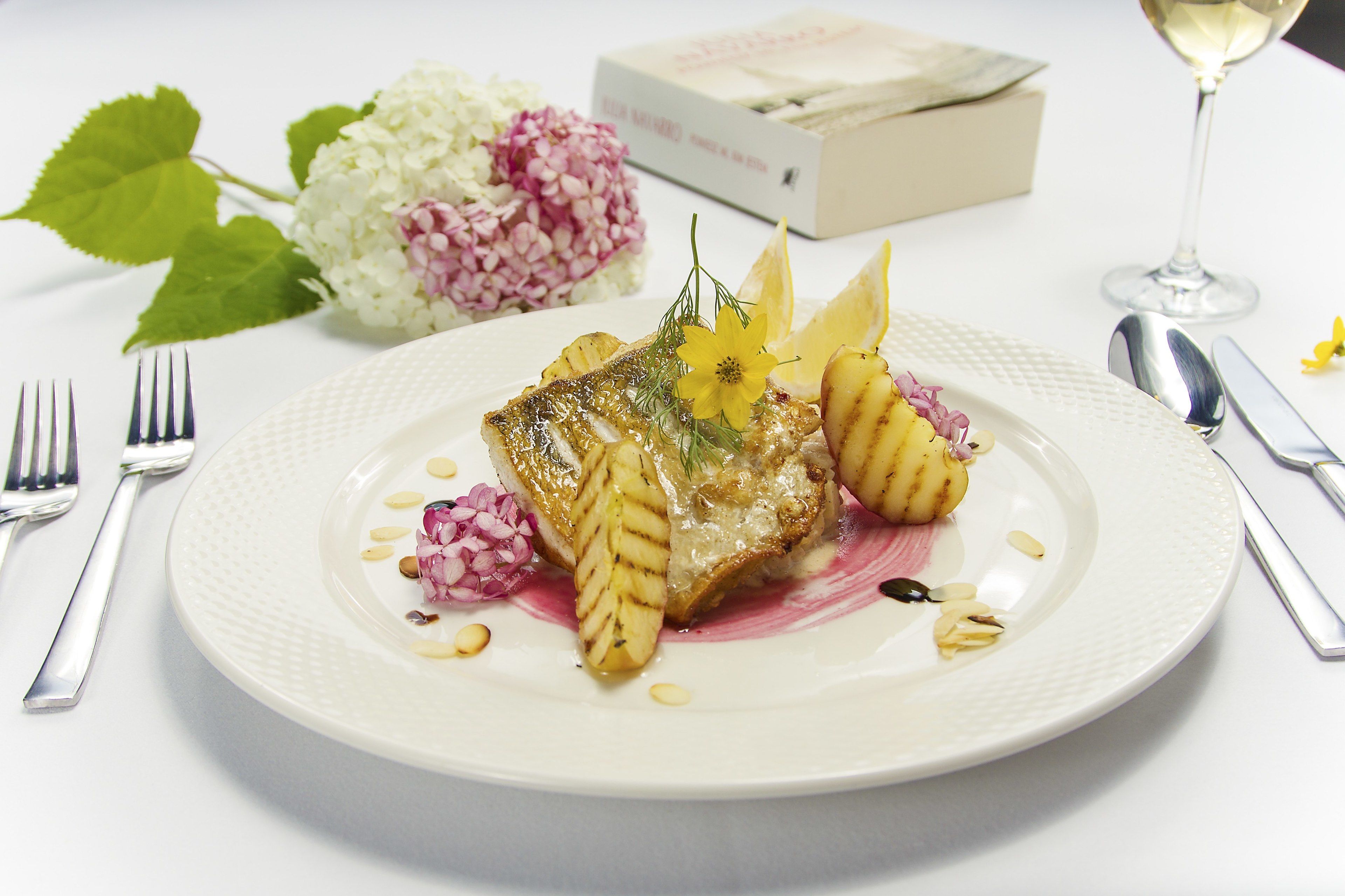 Um prato branco com peixe grelhado, rodelas de limão e um enfeite floral.
