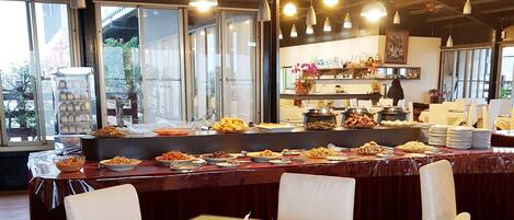 Buffet com diversos pratos, uma pessoa ao fundo e vista para o exterior através de amplas janelas.