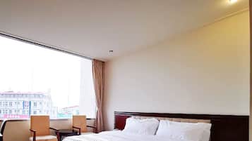 Quarto de hotel com cama, duas cadeiras, janela com cortinas e vista para prédios.