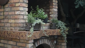 Forno de tijolos ao ar livre com um banco de pedra, plantas em vasos e uma roda.
