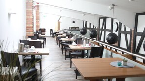 Um restaurante moderno com mesas de madeira e cadeiras pretas, parede de tijolos e arte geométrica na parede.