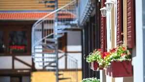 Uma rua estreita com um edifício que apresenta uma escadaria em espiral, caixas com flores e um vaso pequeno.