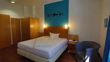 Quarto de hotel com uma cama grande, guarda-roupa de madeira, uma escrivaninha com cadeira e um painel com ilustração de garrafa de vinho.