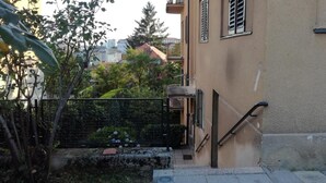 Edifício residencial com portão fechado, pequena área de jardim e escadaria que dá acesso à entrada.