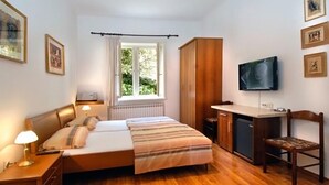 Quarto com cama, mesa de cabeceira, luminária, janela, televisão e uma pequena área de cozinha.