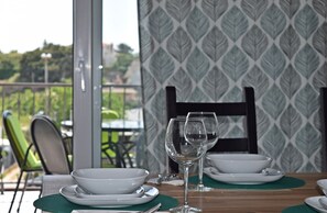Uma mesa de jantar posta com tigelas e pratos brancos, uma taça de vinho e um jogo americano verde.