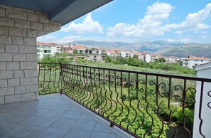 Uma varanda com grade de metal, vista para área residencial com casas e montanhas ao fundo.