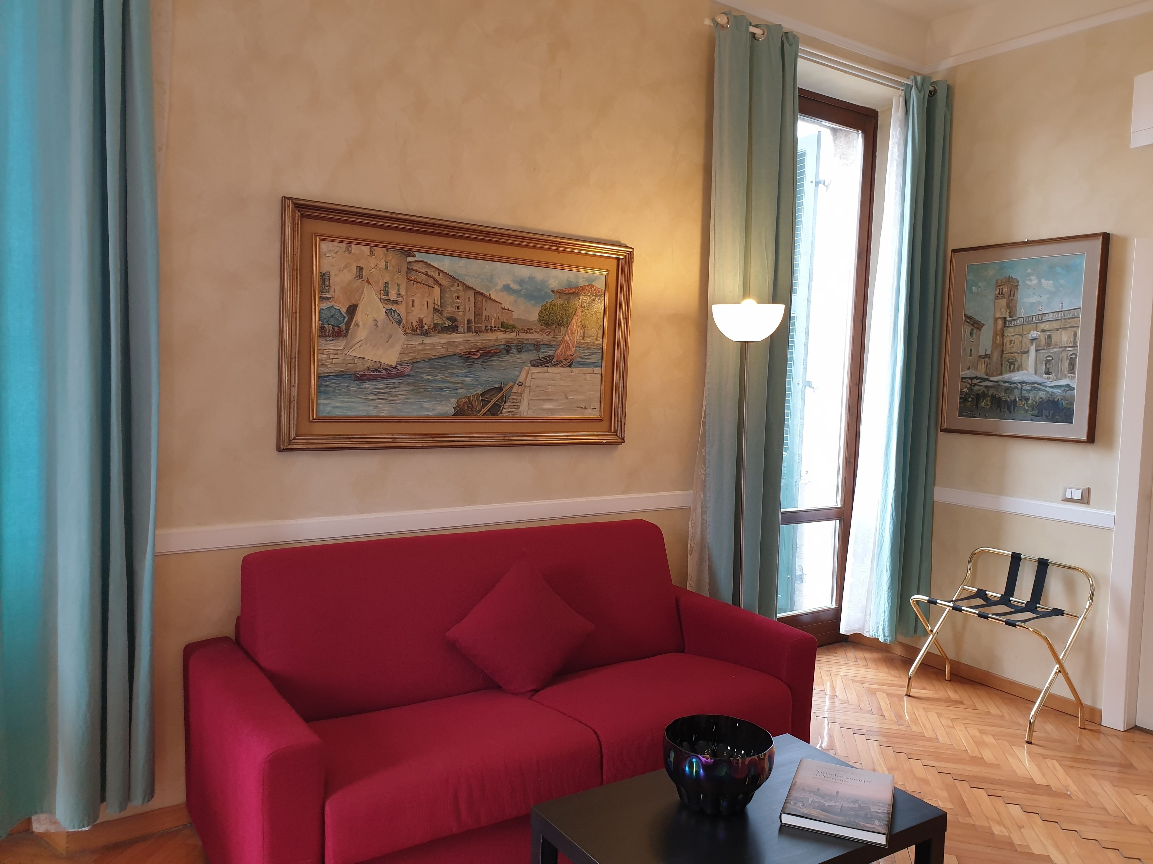 Um quarto com um sofá vermelho, uma mesa de centro de madeira, uma tigela preta e duas pinturas na parede.